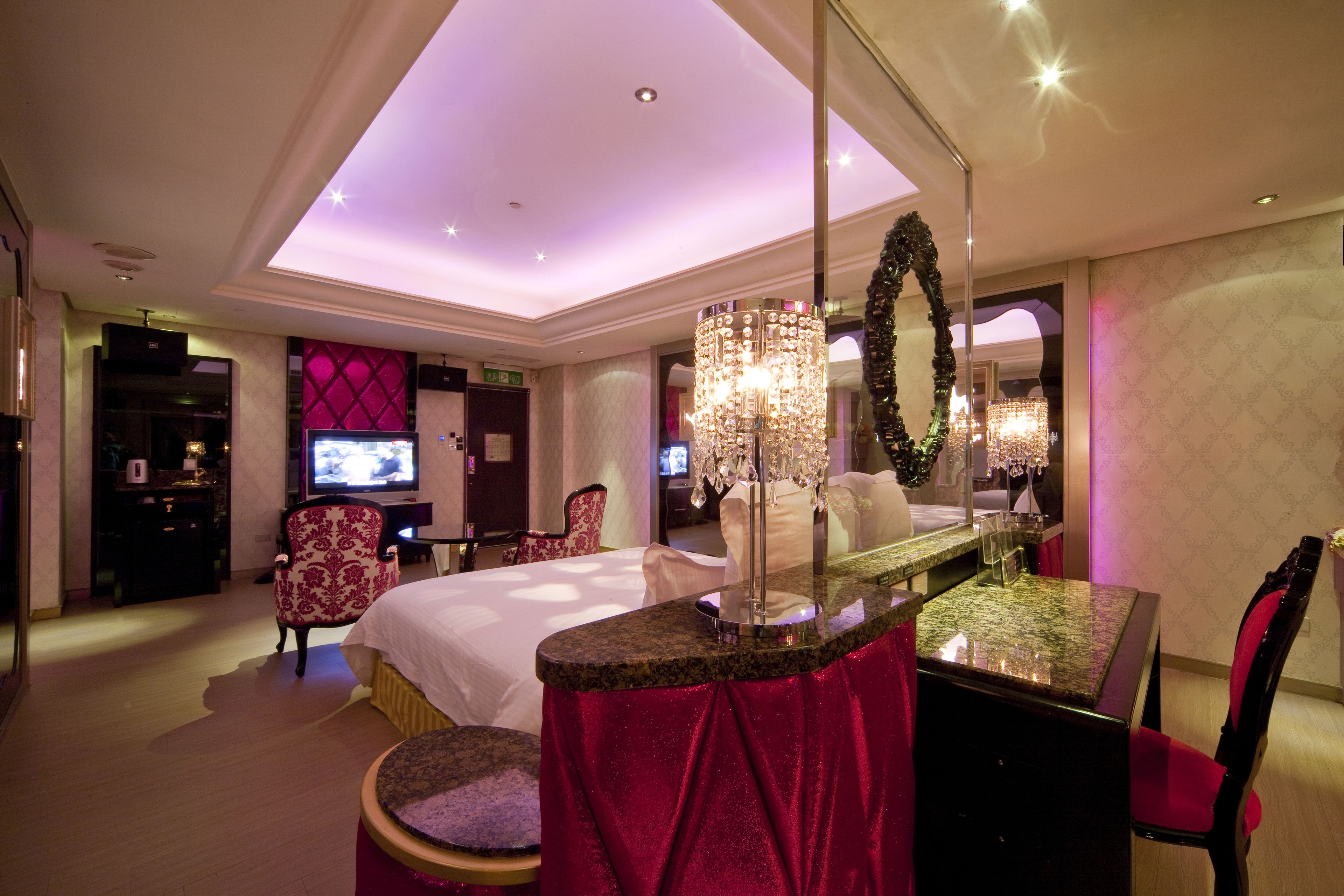 Quarto de hotel com cama, escrivaninha com computador, televisão e lustre.