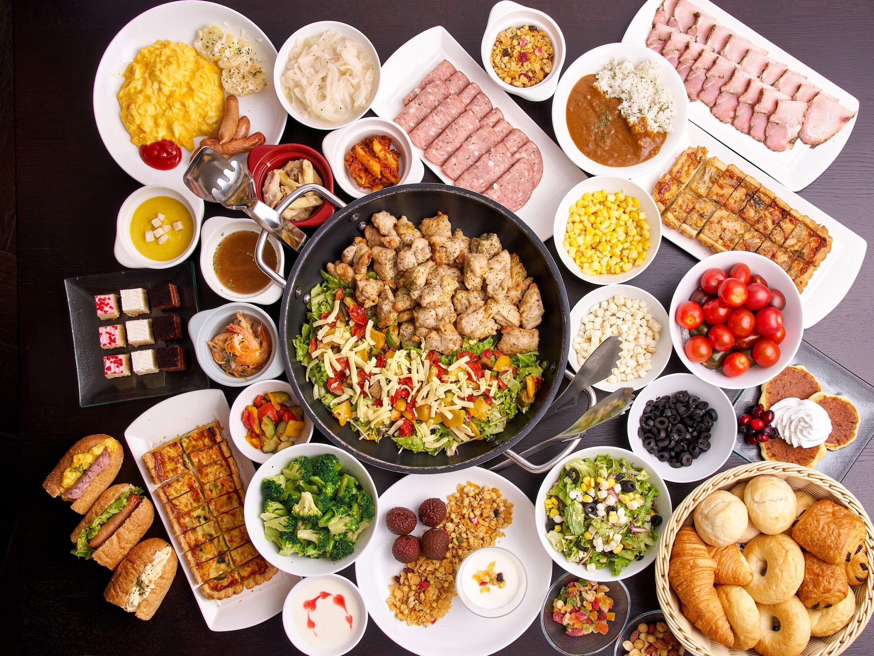 Diversos pratos, incluindo ovos mexidos, salsichas e uma salada com frango grelhado.