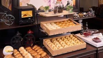 Uma mesa de buffet com diversos produtos de pastelaria, uma máquina de café e uma parede decorativa.