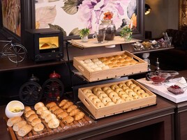 Uma mesa de buffet com diversos produtos de pastelaria, uma máquina de café e uma parede decorativa.