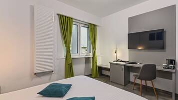 Quarto de hotel moderno com uma cama, escrivaninha, cadeira, televisão e janela com cortinas.