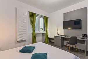 Quarto de hotel moderno com uma cama, escrivaninha, cadeira, televisão e janela com cortinas.