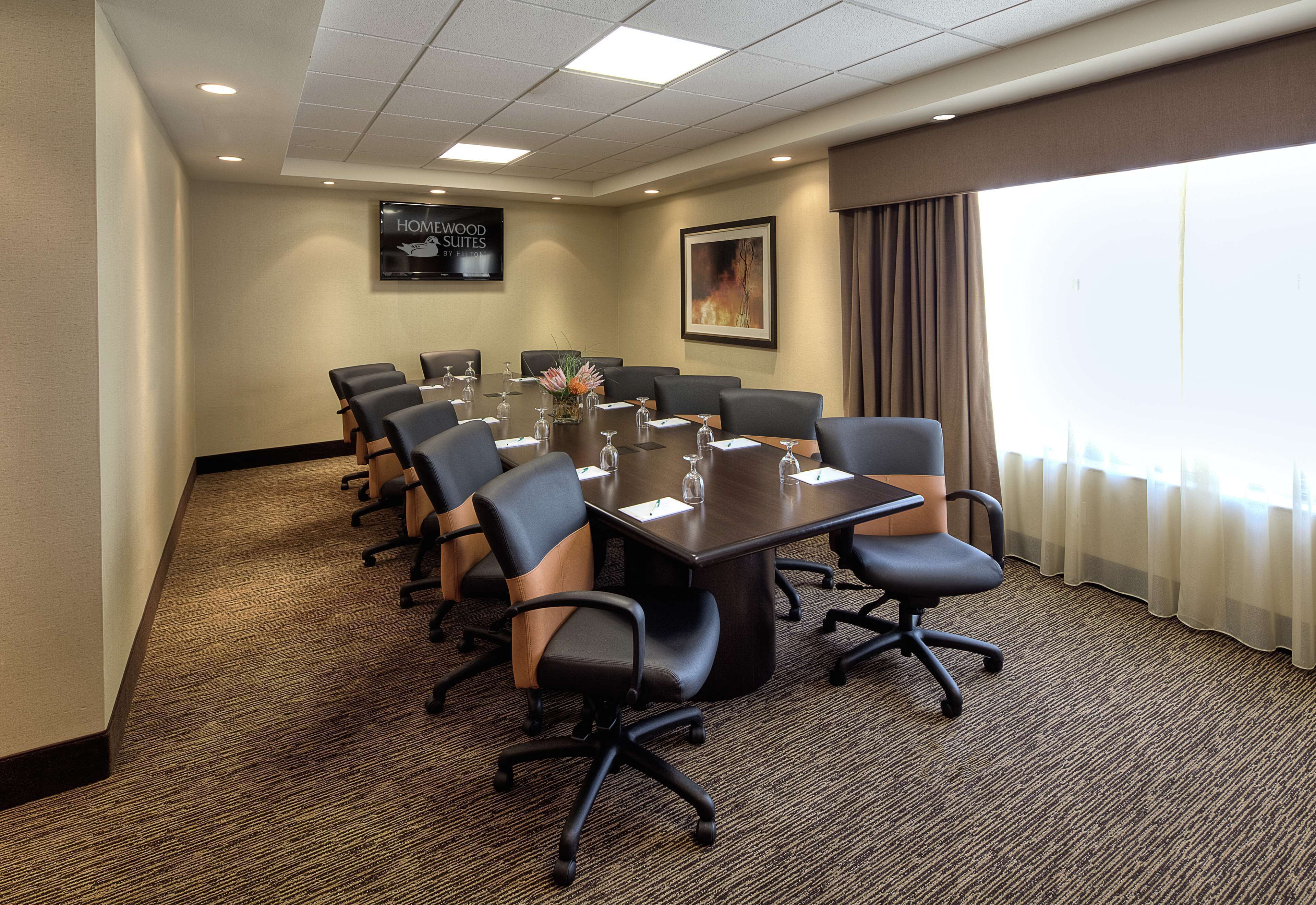 Sala de conferência com uma mesa comprida, várias cadeiras e um grande janela com cortinas.