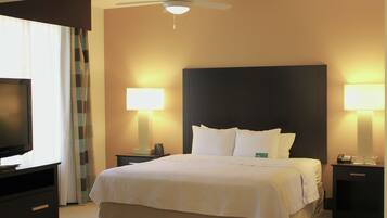 Quarto de hotel com cama, duas luminárias laterais, TV, ventoinha no teto e mesa de cabeceira com telefone.