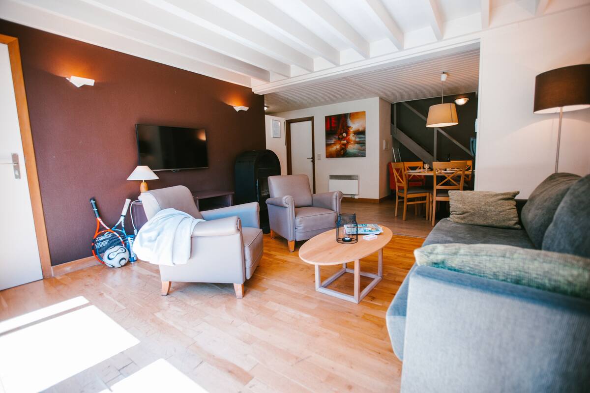 Uma sala de estar moderna com um sofá, poltronas, uma mesa de centro e uma televisão.