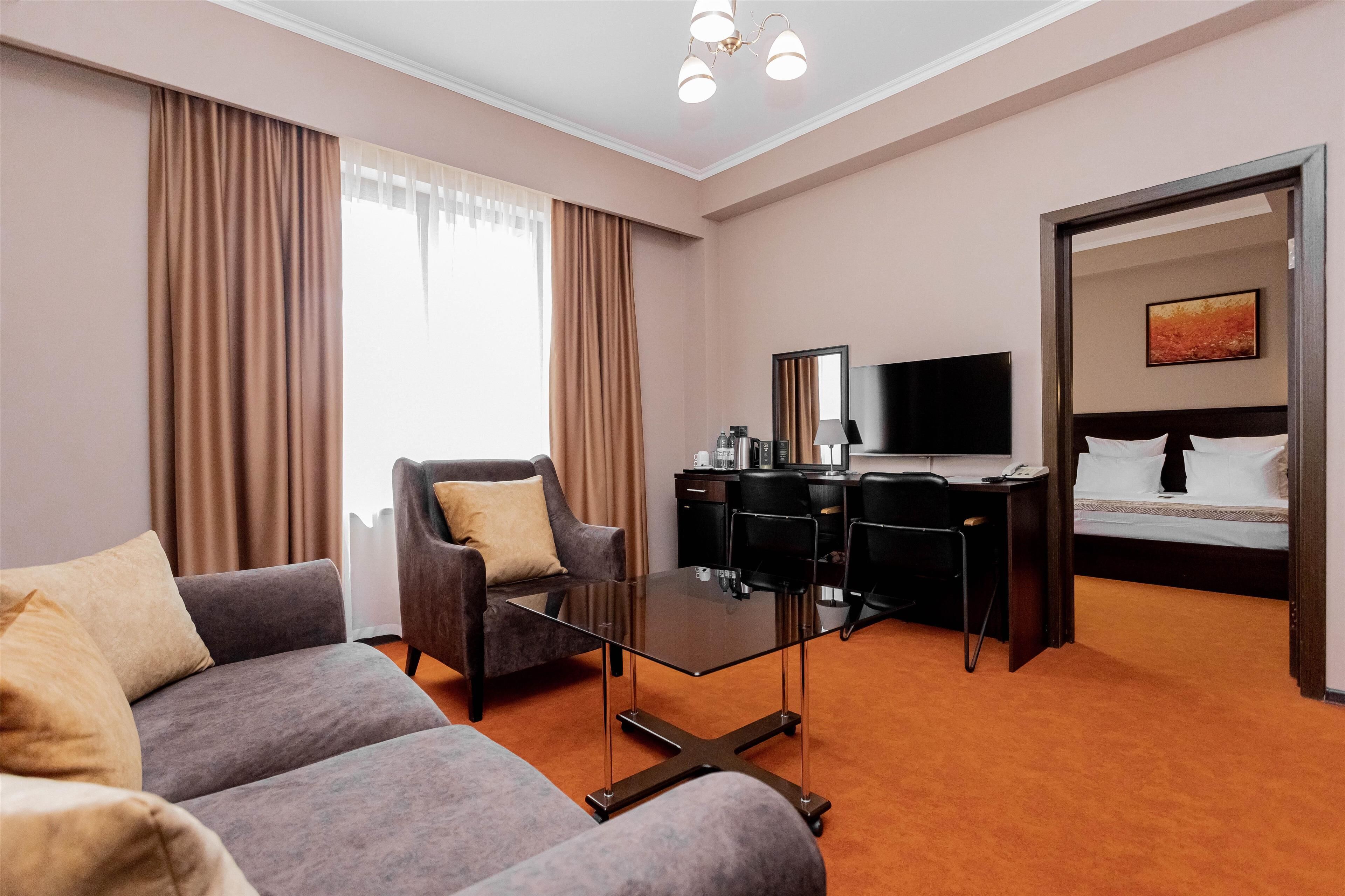 Quarto de hotel com sofá, escrivaninha, cama, televisão e um quadro na parede.