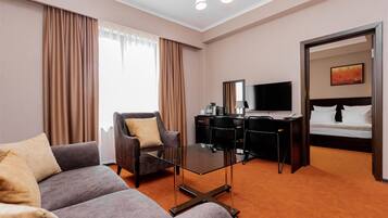 Quarto de hotel com sofá, escrivaninha, cama, televisão e um quadro na parede.