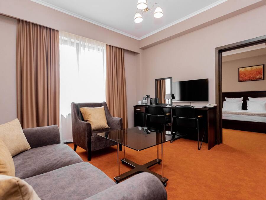 Quarto de hotel com sofá, escrivaninha, cama, televisão e um quadro na parede.