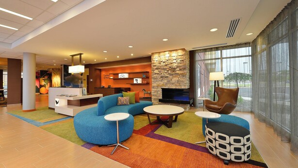Um hall moderno com um sofá modular, mesas redondas, lareira e uma parede de destaque em pedra.