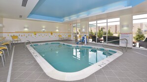 Uma piscina interior com água cristalina, rodeada por cadeiras amarelas e chão em azulejos.
