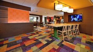 Um hall de hotel com um tapete colorido, uma mesa de recepção e um espaço de bar com cadeiras.