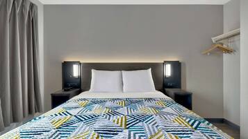 Quarto de hotel com cama, duas mesas de cabeceira, encosto e um cabideiro.