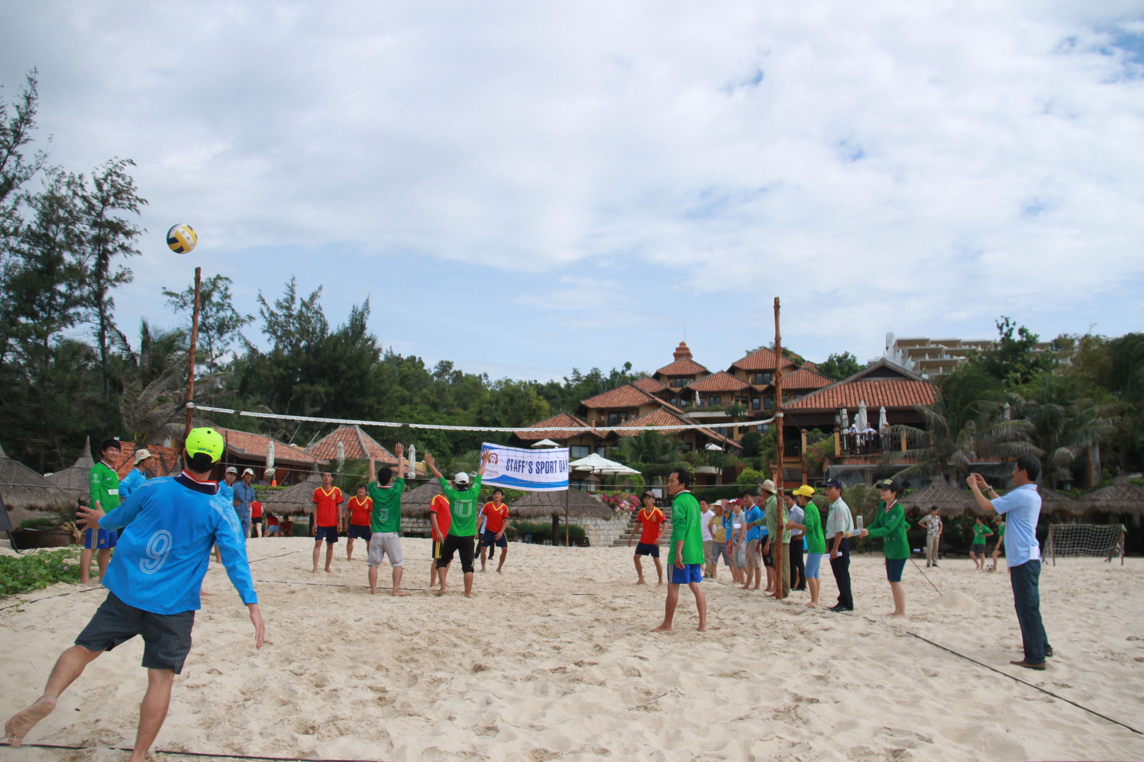 Jogo de voleibol de praia com jogadores vestindo camisas de cores diversas.