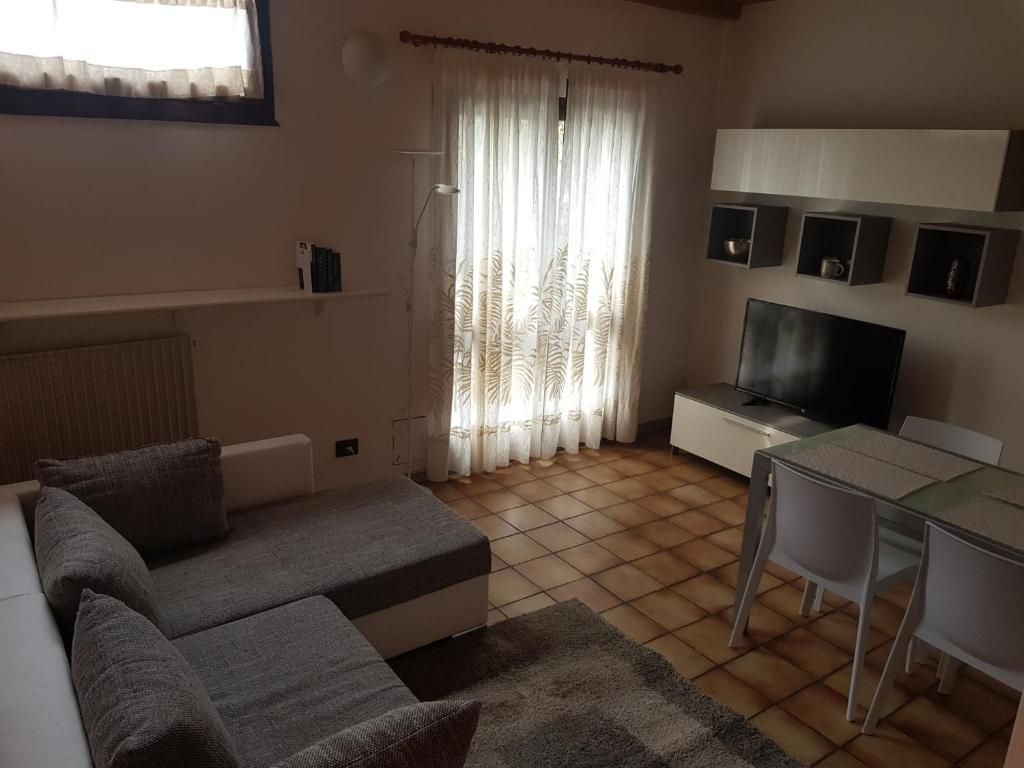 Uma sala de estar com sofá, mesa de jantar com cadeiras, televisão e janela com cortinas.