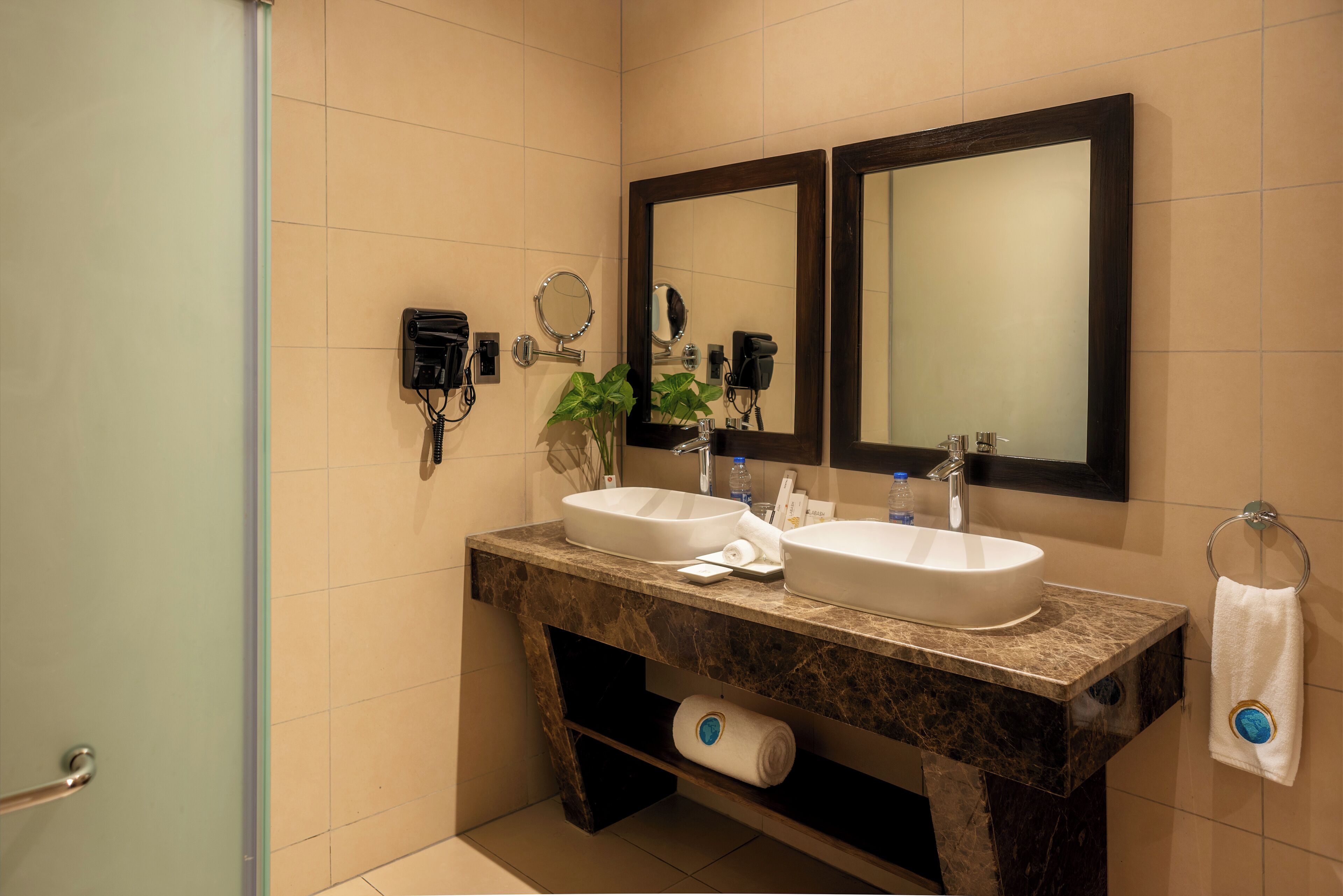 Casa de banho com duas pias, um espelho grande, um secador de cabelo e um porta-toalhas.