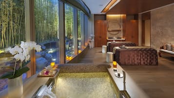 Um spa moderno com uma janela grande, uma banheira de hidromassagem e um espaço de estar com vista para uma floresta de bambu.