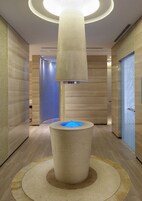 Um lobby moderno com uma coluna cilíndrica central, uma área de estar circular e uma parede com iluminação azul.