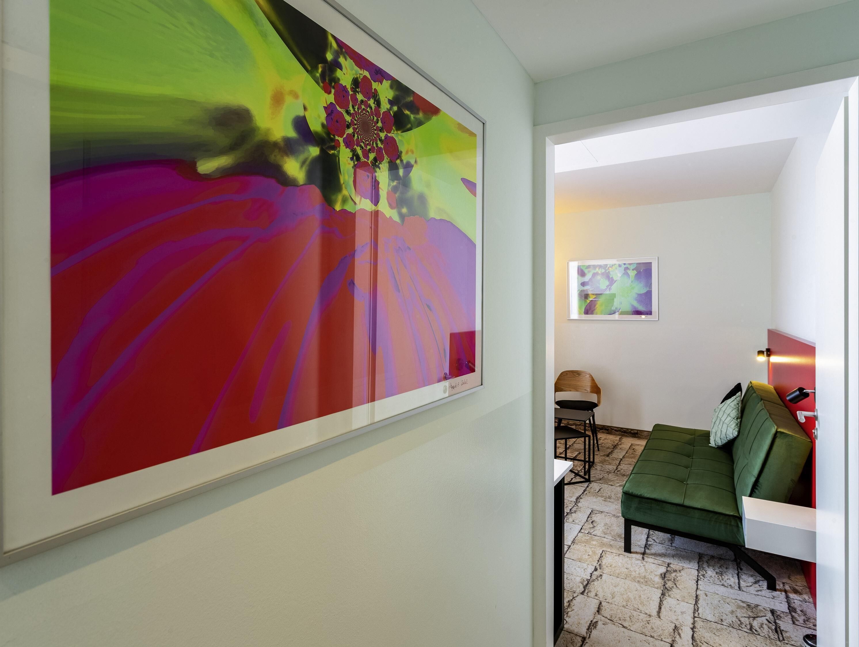 Uma sala de estar moderna com um grande quadro abstrato, um sofá verde, uma mesinha e uma cadeira.
