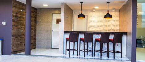 Uma área de bar ao ar livre com quatro banquetas, duas luminárias pendentes e um balcão de mármore.