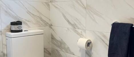 Um banheiro com vaso sanitário, rolo de papel higiênico e toalha pendurada na parede.
