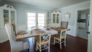 Uma sala de jantar com uma mesa de madeira, cadeiras brancas e um lustre.