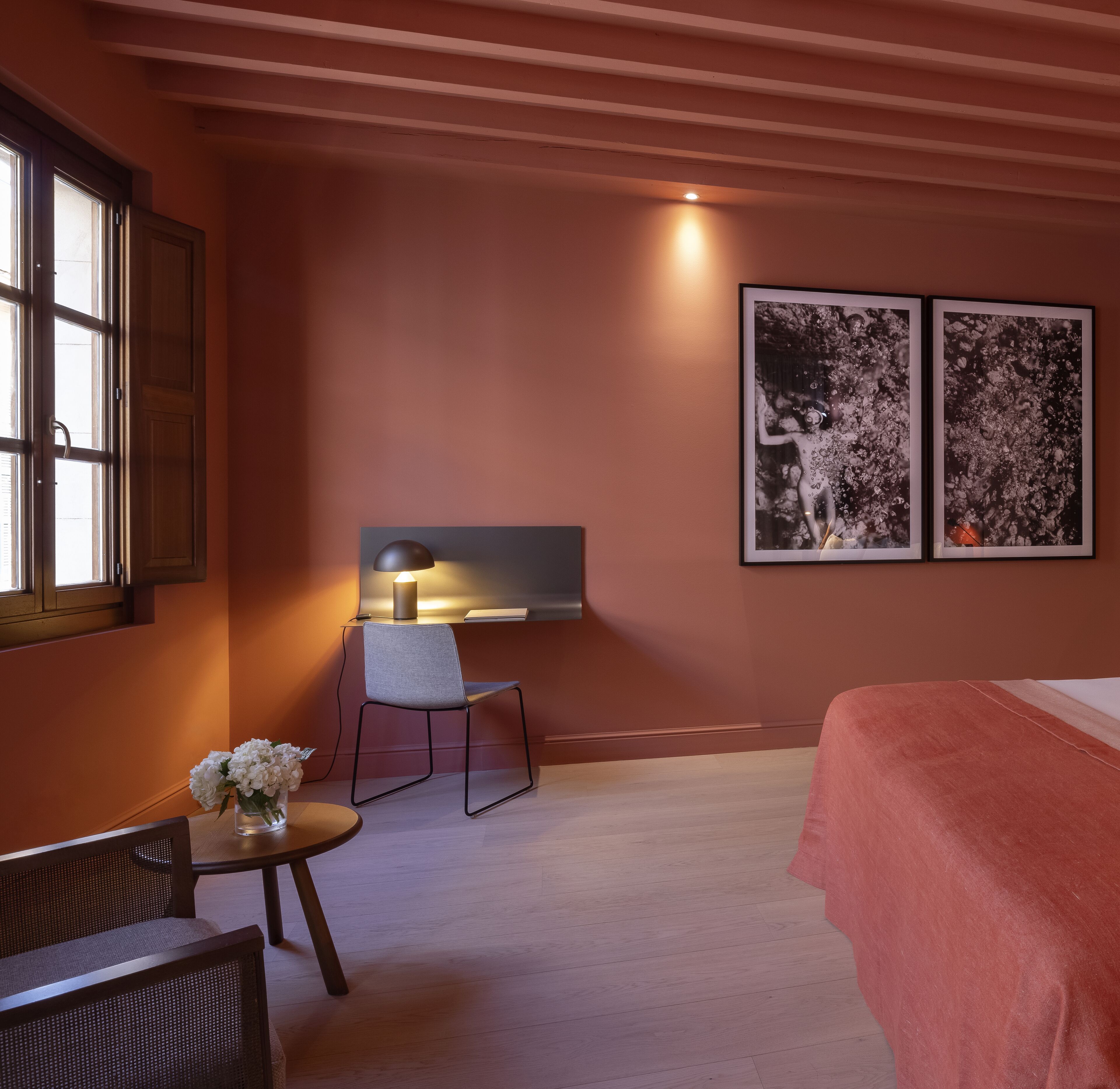Quarto com cama, escrivaninha com cadeira, luminária e duas imagens emolduradas na parede.