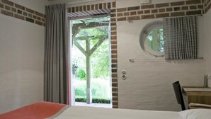 Quarto com cama, janela com cortinas, espelho redondo e mesa de cabeceira de madeira.