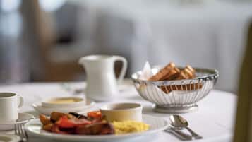 Uma mesa de café da manhã com pratos de comida, uma cesta de torradas, um jarro e uma xícara.