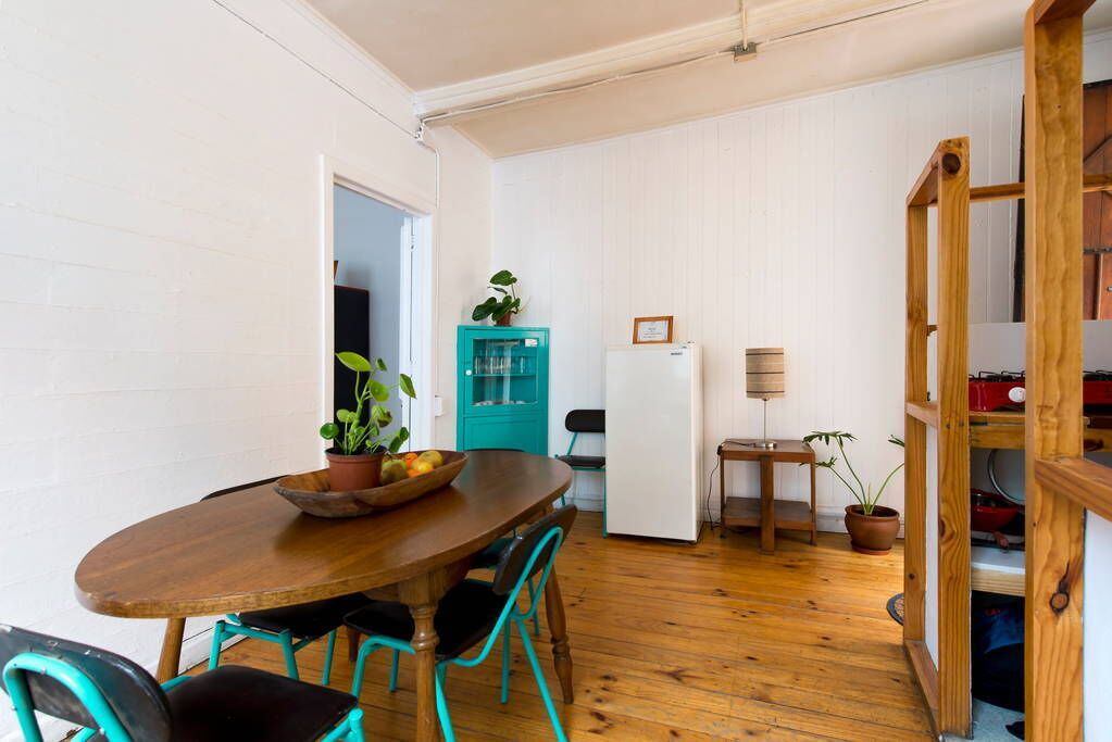 Uma sala de jantar com mesa e cadeiras de madeira, um armário verde-água, um refrigerador e uma estante de livros de madeira.