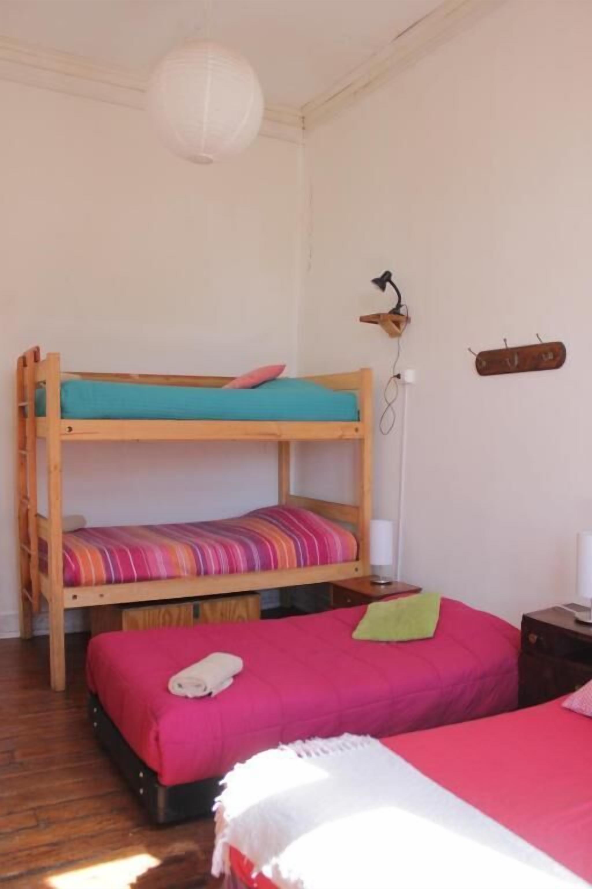 Quarto com beliche de madeira, uma cama de solteiro embaixo e uma escrivaninha com luminária.