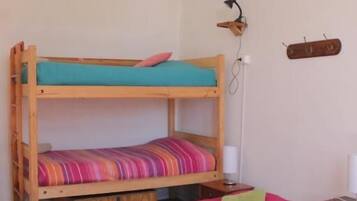 Quarto com beliche de madeira, uma cama de solteiro embaixo e uma escrivaninha com luminária.