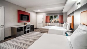 Quarto de hotel com duas camas, uma escrivaninha, televisão e janela com cortinas.
