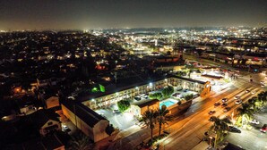 Um hotel com vários andares, piscina, estacionamento e vista para a cidade à noite.