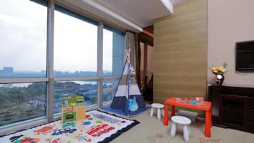 Um apartamento alto com grandes janelas, uma tenda de brincar, uma mesa de recreação infantil e vista para a paisagem urbana.