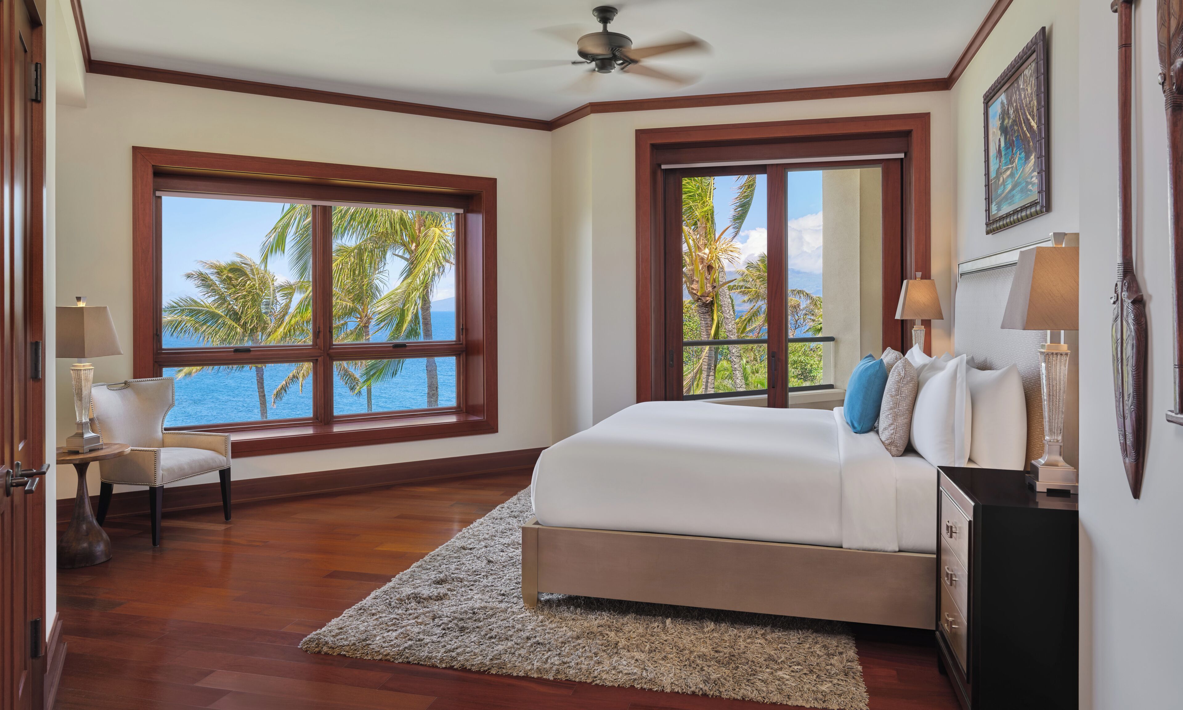 Quarto com uma grande janela, cama, ventilador de teto e vista para o oceano.