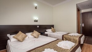 Quarto de hotel com duas camas, cada uma com cabeceira, roupa de cama branca e almofadas estampadas. Um criado-mudo com abajur e telefone fica ao lado de uma das camas.