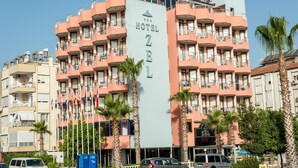 Um hotel com vários andares, varandas, palmeiras e uma placa com a inscrição 'HOTEL ZEL'.