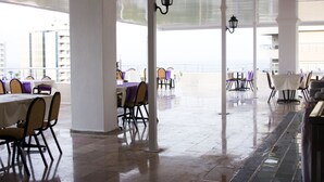 Um espaço de refeições em ambiente interno com mesas, cadeiras, colunas imponentes e lanternas penduradas.