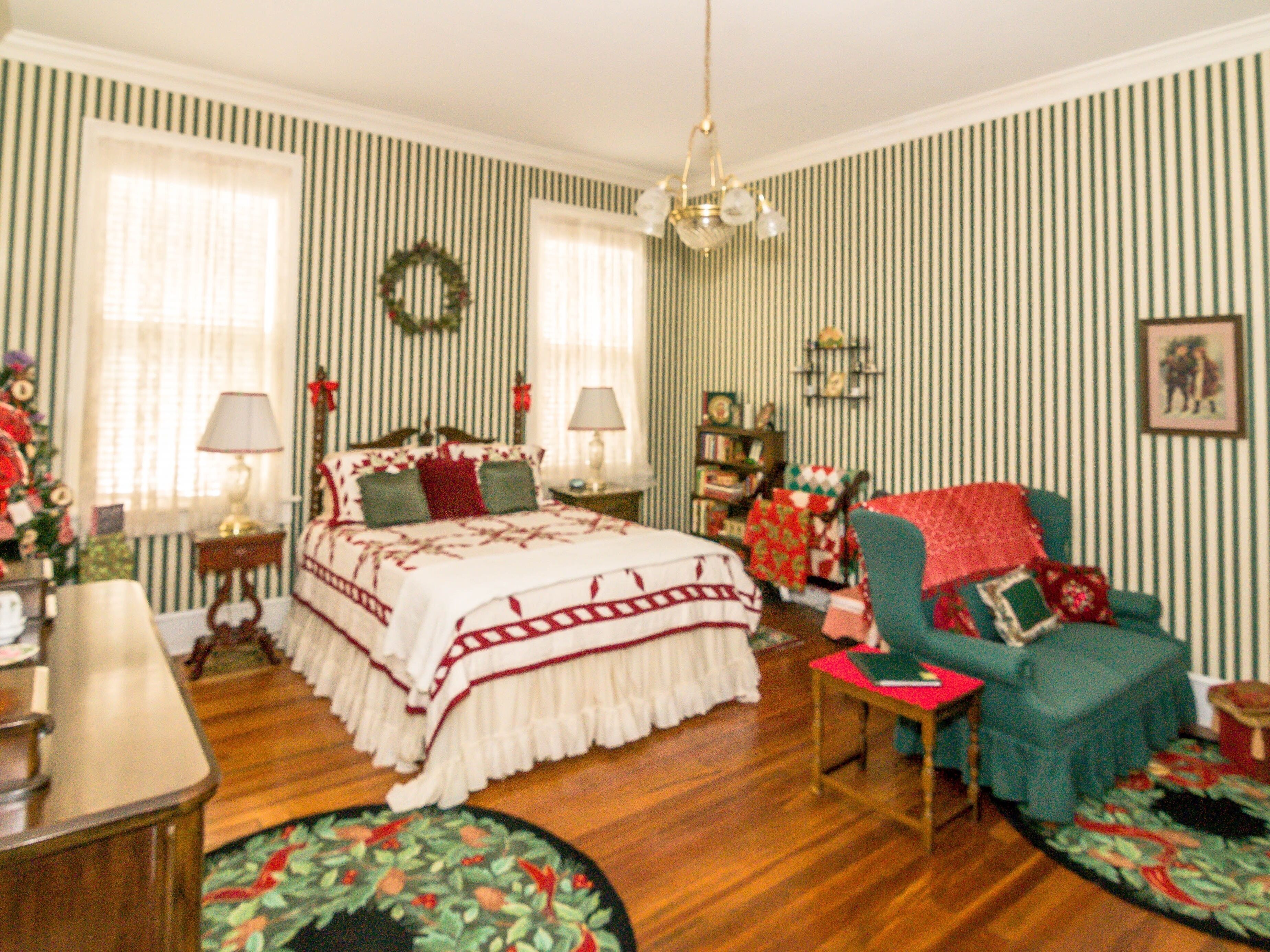 Um quarto com uma cama, uma poltrona verde, uma mesa pequena, uma estante de livros e uma lareira.