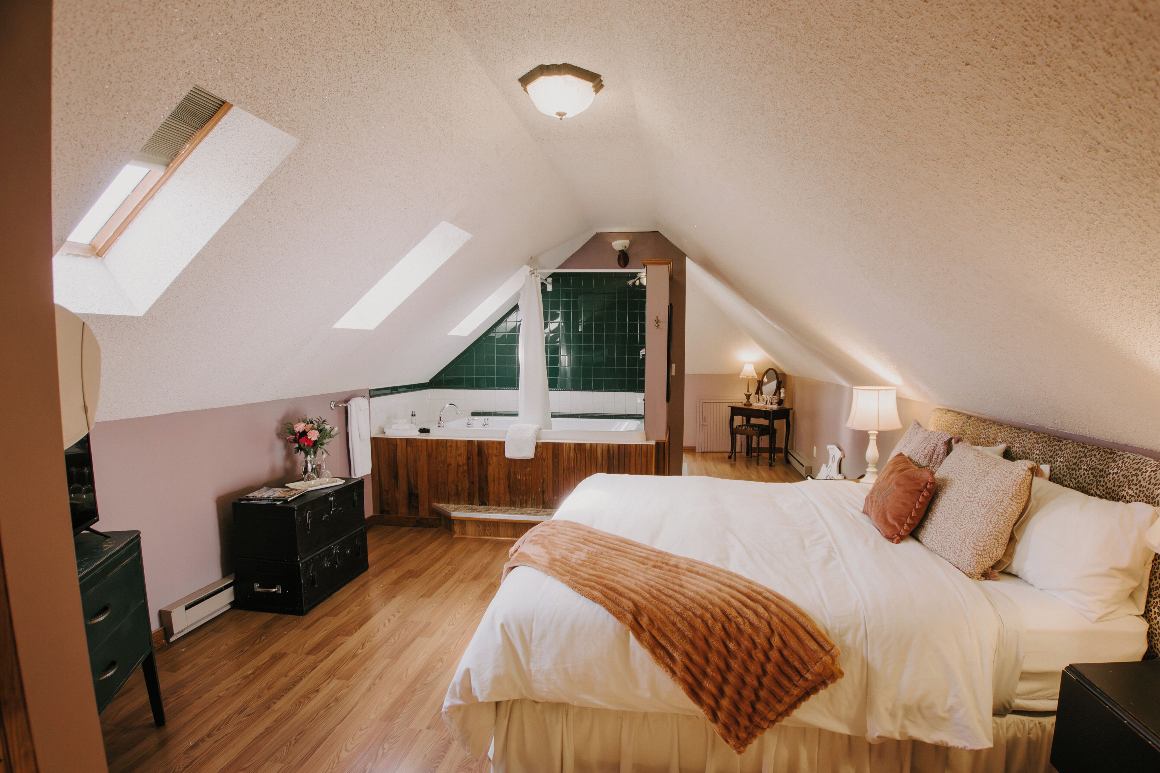 Quarto com uma cama grande, cômoda de madeira, penteadeira e banheiro com banheira.
