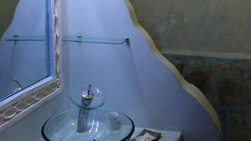 Um banheiro com pia de vidro, chuveiro e espelho com moldura decorativa.