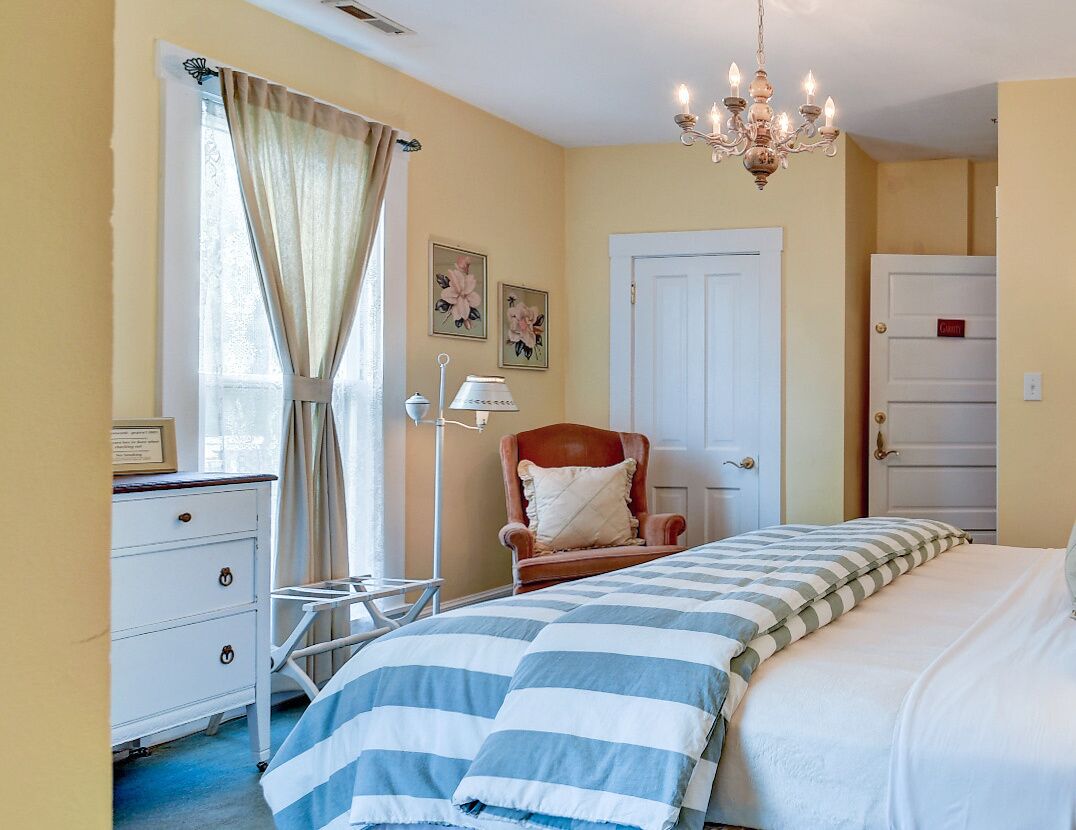 Quarto com cama, uma cadeira, escrivaninha e lustre.