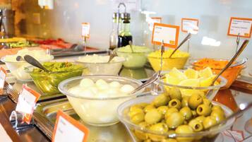 Buffet com diversos alimentos, incluindo azeitonas, fatias de limão e uma tigela com comida branca.