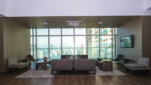 Um espaço de escritório moderno com uma janela grande, dois sofás, uma mesa pequena e uma cadeira.