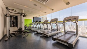 Uma academia com esteiras, aparelhos de musculação e uma grande janela com vista para a cidade.