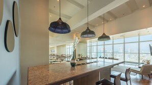 Uma área de bar moderna, com um balcão comprido, luminárias pendentes e vista da cidade por grandes janelas.