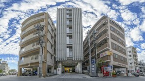 Um edifício com vários andares, entrada central, estacionamento e espaços comerciais no térreo.