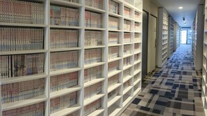 Uma biblioteca com estantes forrando um corredor com piso coberto por carpete estampado.