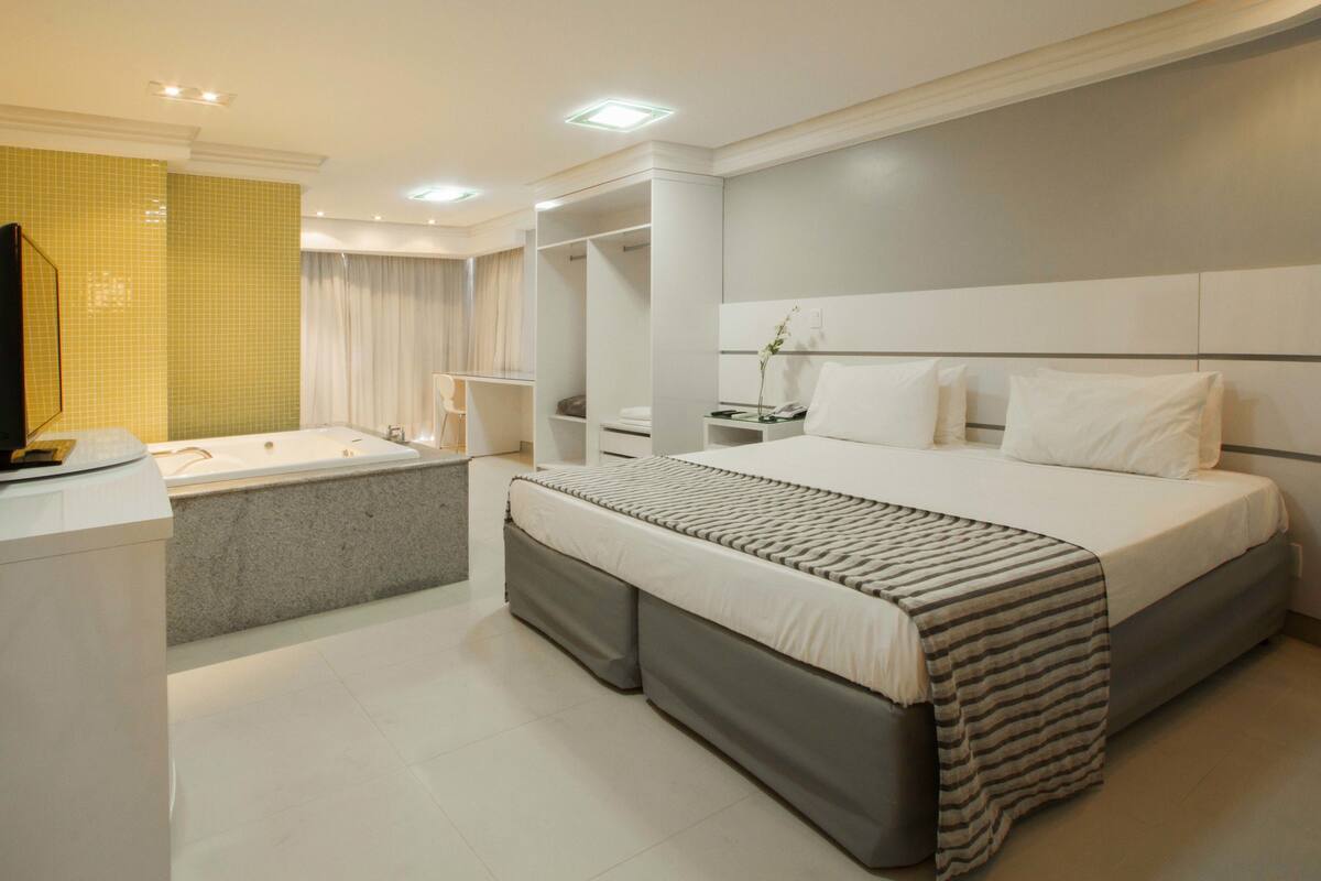 Quarto de hotel moderno com uma cama grande, banheiro separado com banheira e toucador com espelho.