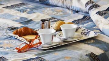 Uma bandeja com croissants, duas xícaras e um pequeno recipiente sobre uma cama com colcha estampada.